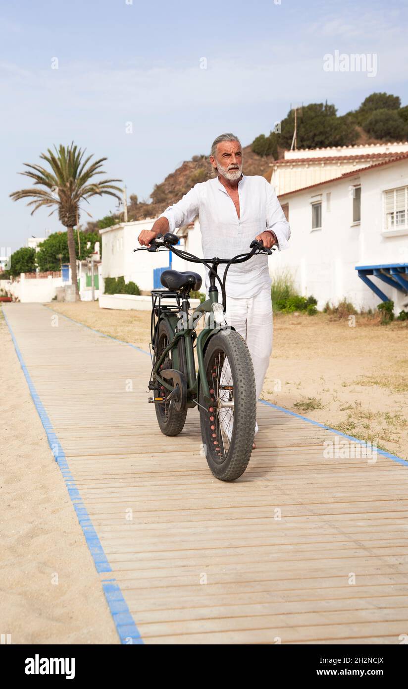 Mature man wheeling bicycle on boardwalk Stock Photo - Alamy