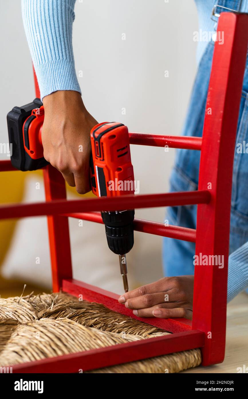 Young Afro woman with electric screwdriver repairing chair at home ...