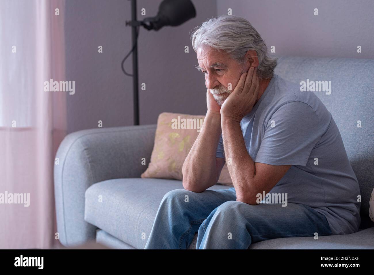 Sad man with hands on chin sitting at home Stock Photo - Alamy