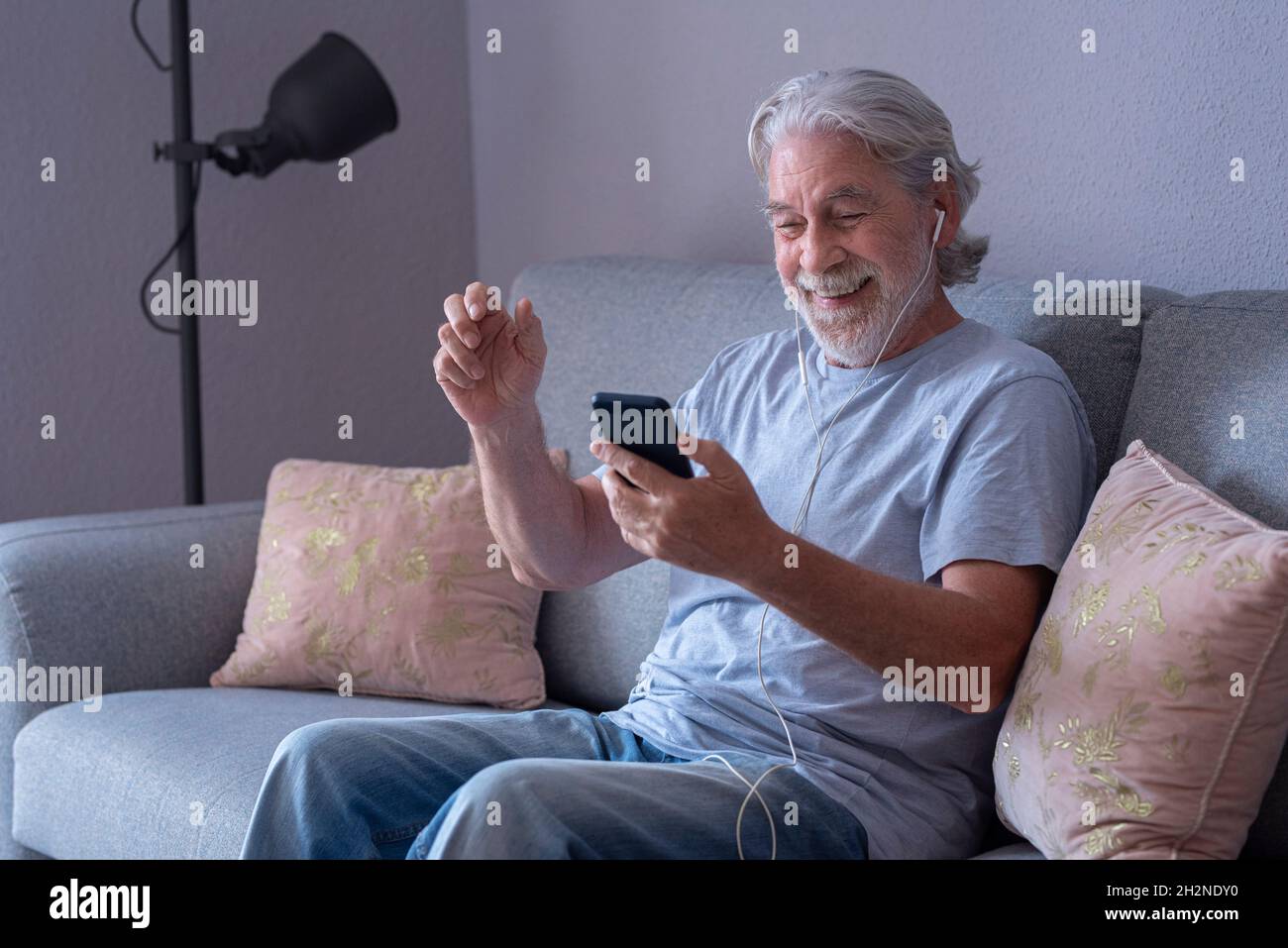 Cheerful man attending video call through smart phone in living room ...