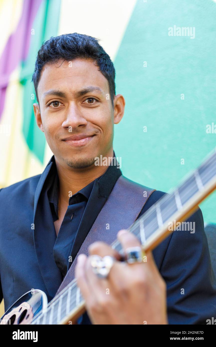 Male musician playing guitar while standing in front of colorful wall ...