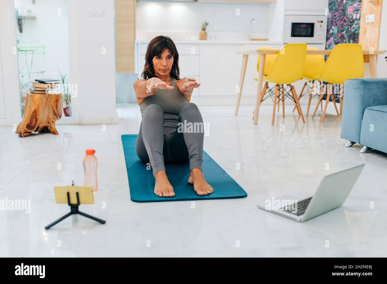 Mature female influencer doing yoga while vlogging in living room at ...