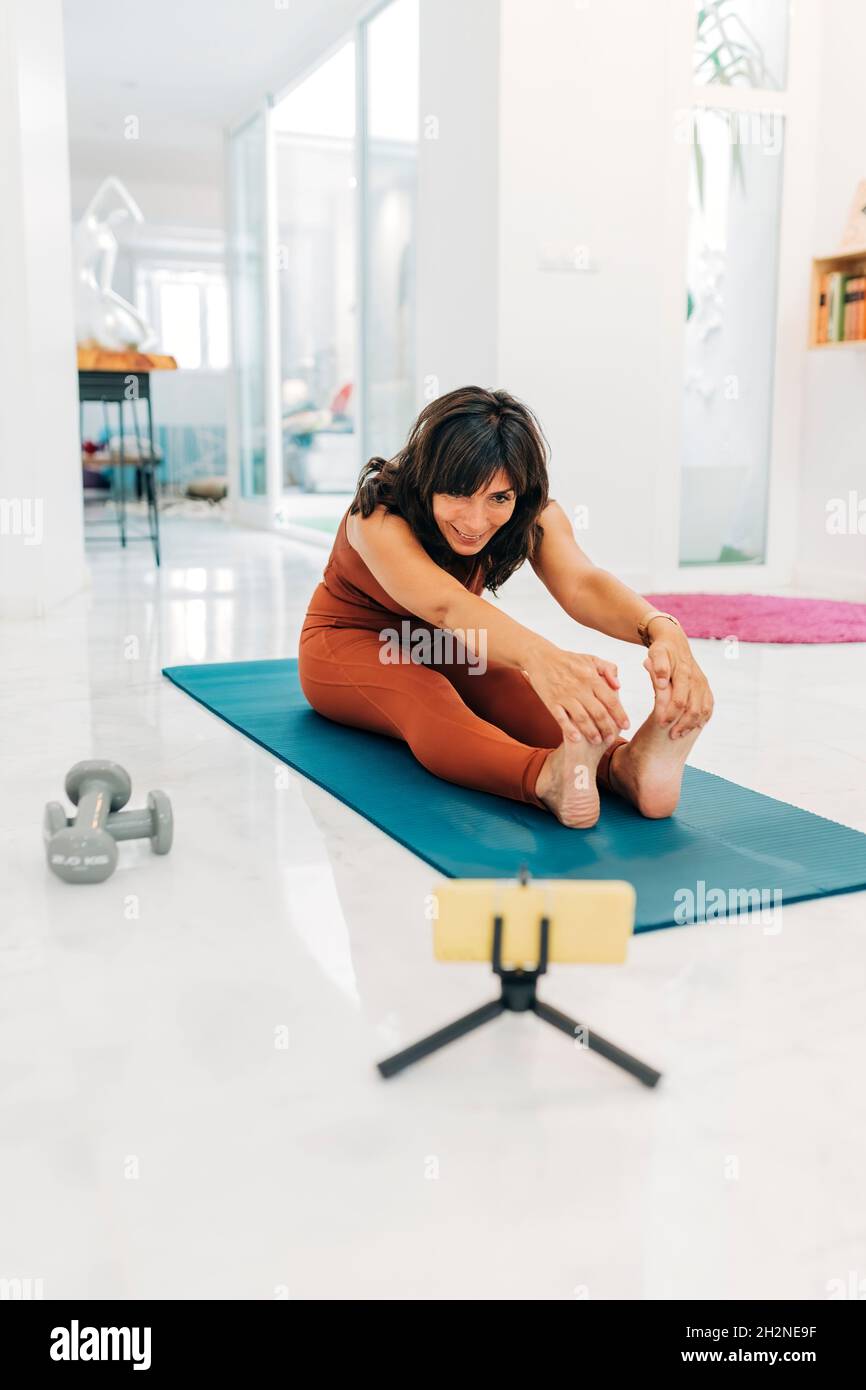 Female influencer doing yoga while vlogging through mobile phone at ...