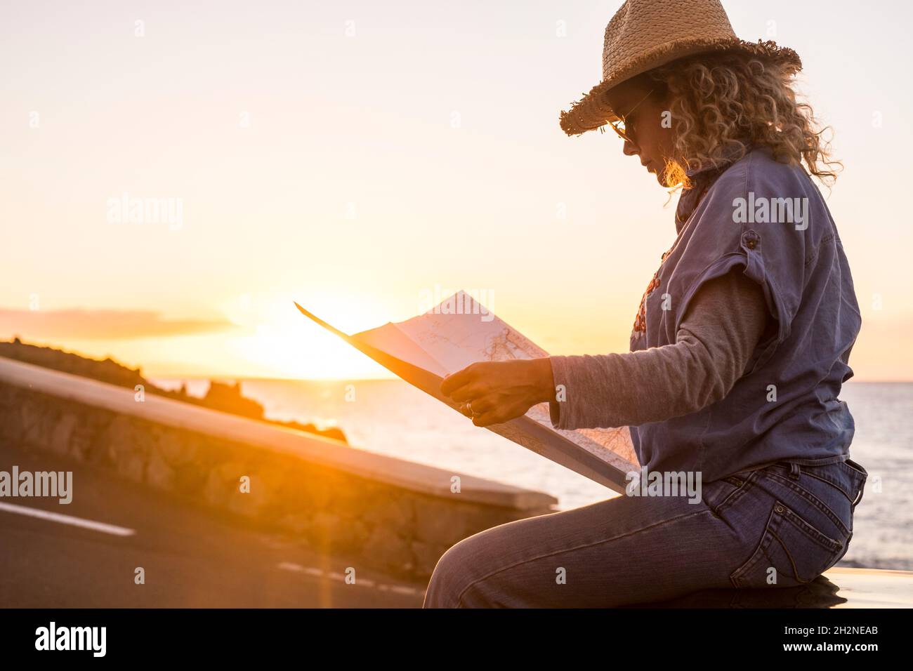 Woman reading map while sitting on car at beach Stock Photo - Alamy