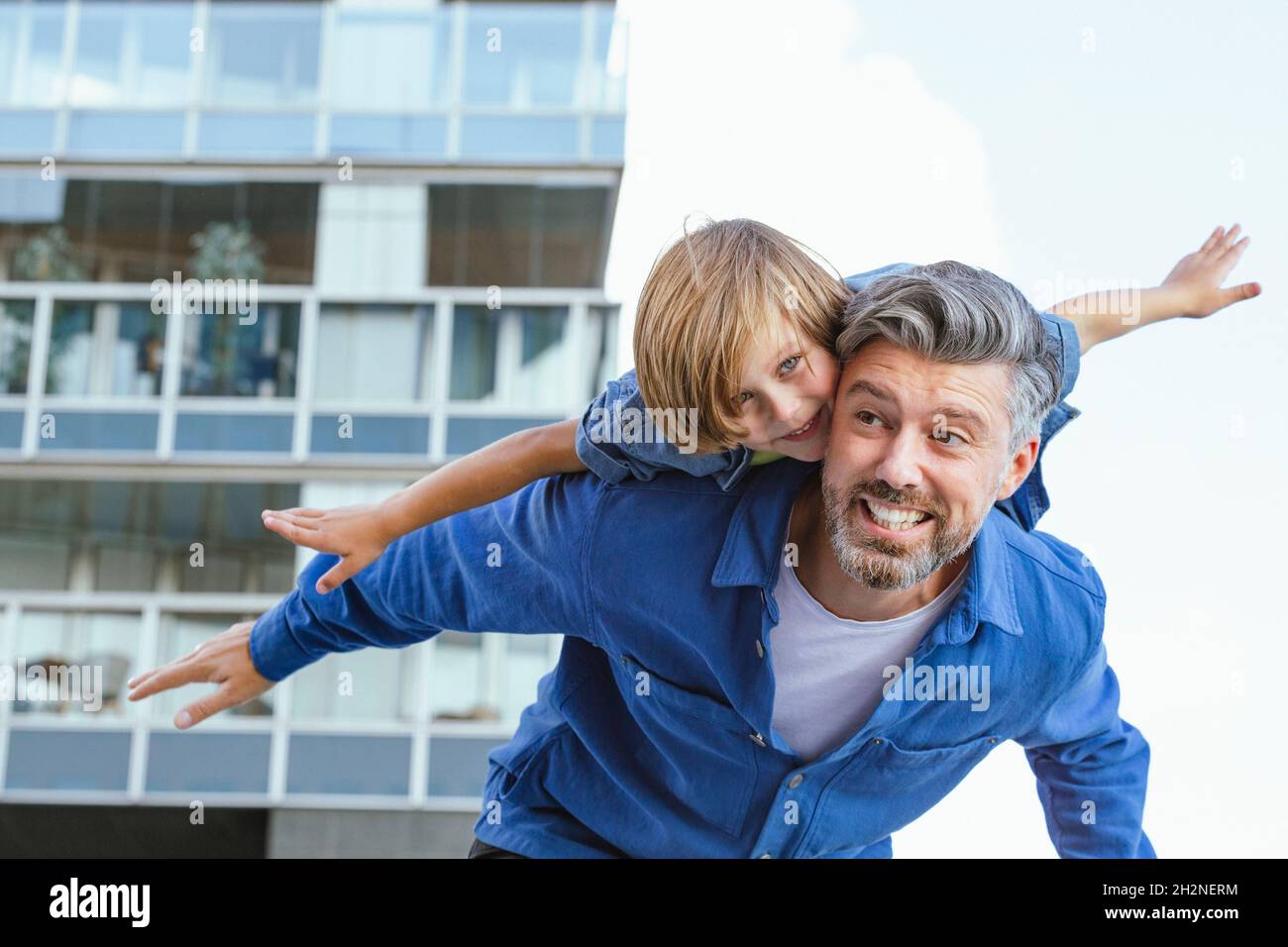 Father standing behind playful son with arms outstretched at railing ...