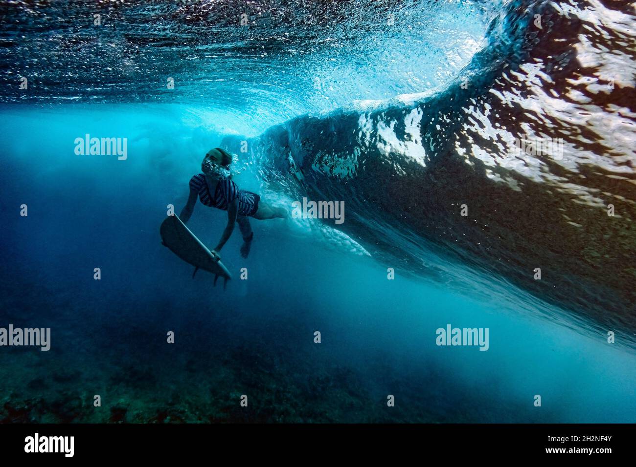 Woman with surfboard diving under waves Stock Photo - Alamy