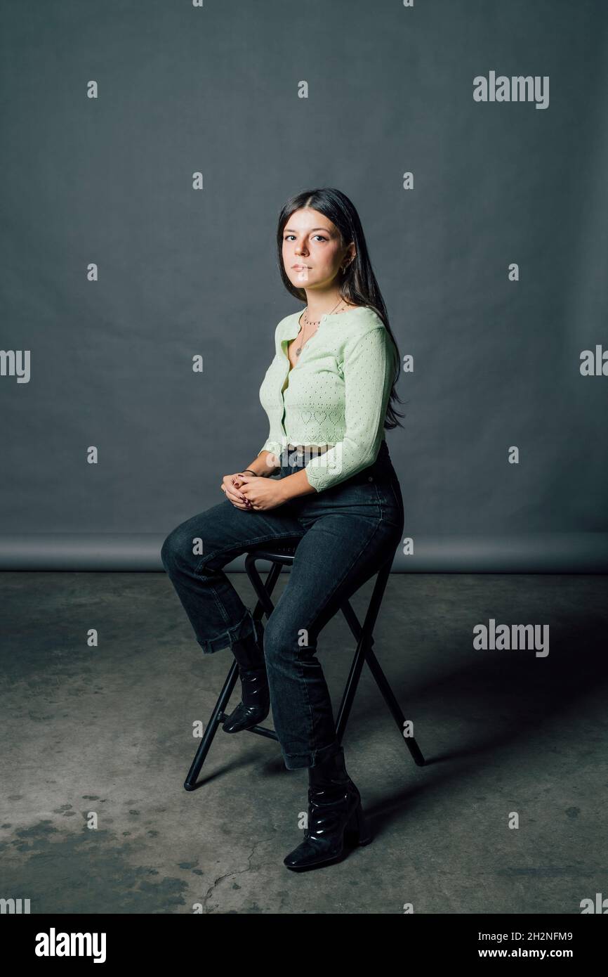 Confident young woman sitting on chair in studio Stock Photo - Alamy