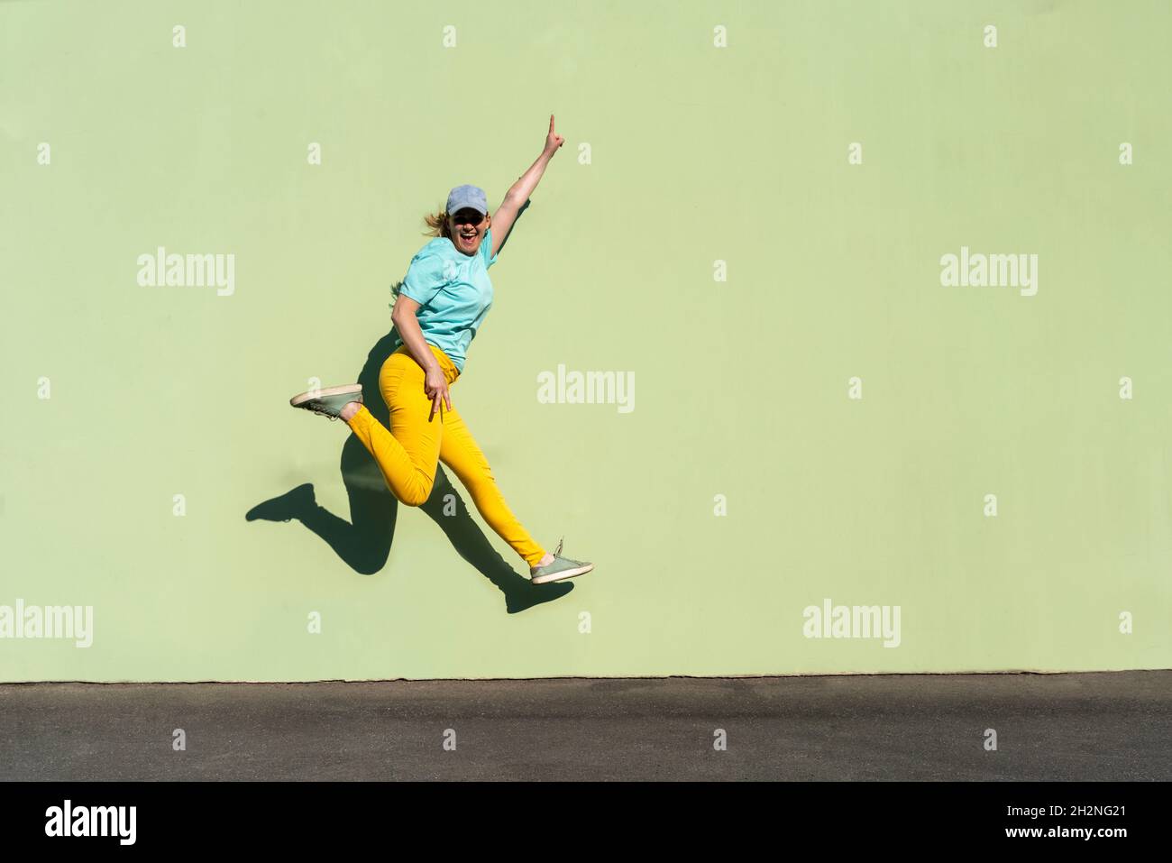 Happy woman with hand raised jumping by green wall Stock Photo - Alamy