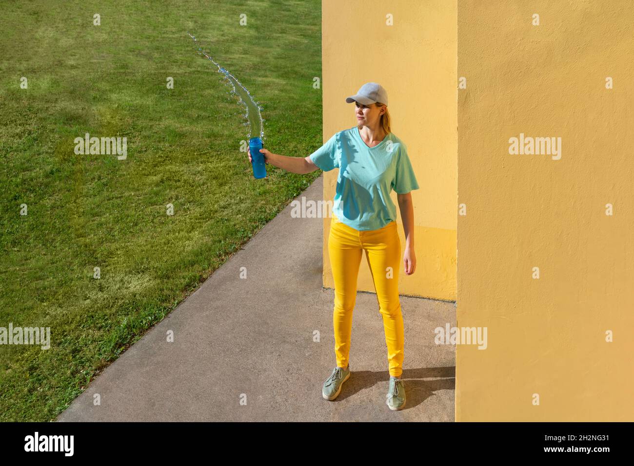 Woman throwing water while standing by yellow wall Stock Photo - Alamy