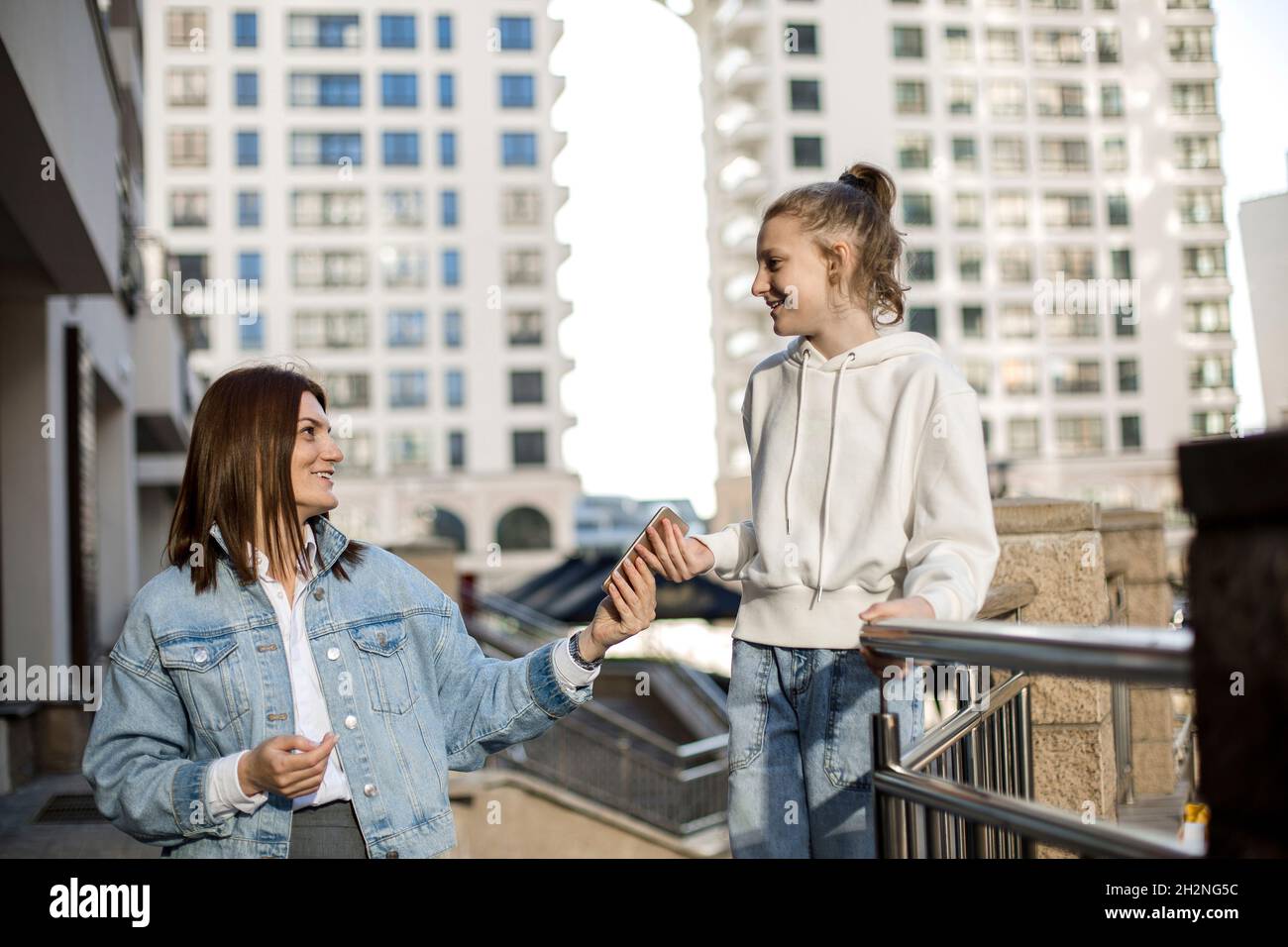Mother giving mobile phone to daughter standing at railing Stock Photo ...