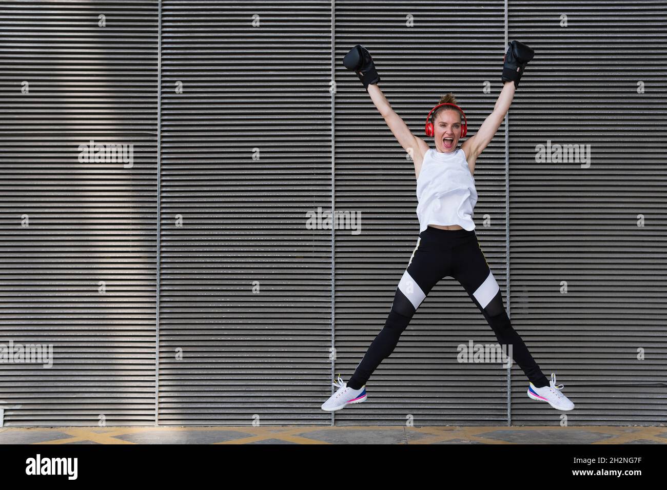 Cheerful female boxer jumping with arms raised in front of wall Stock ...