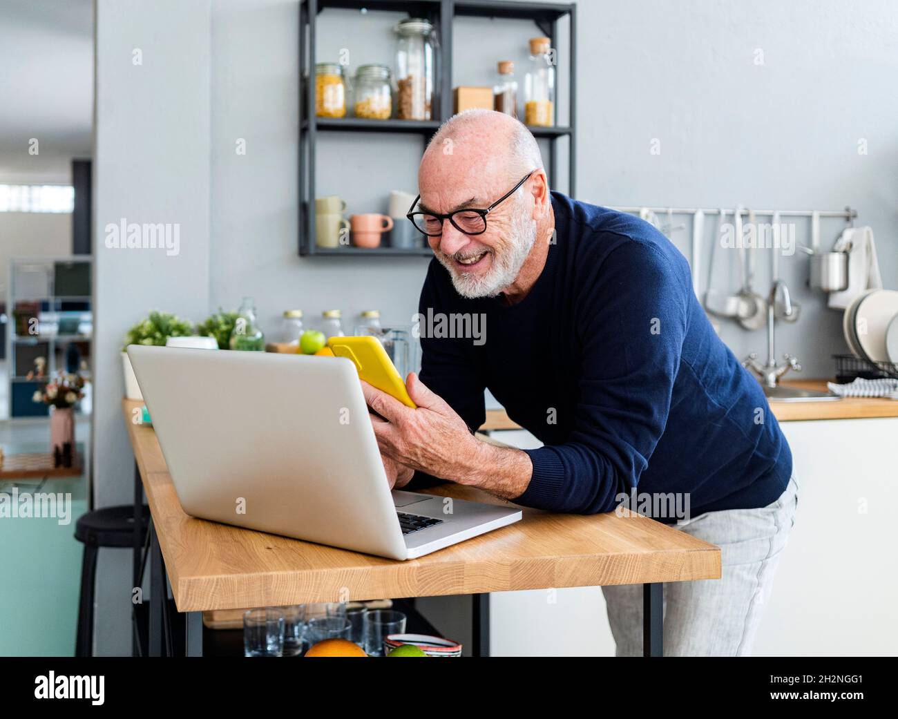 Smiling man with laptop leaning on kitchen counter Stock Photo - Alamy
