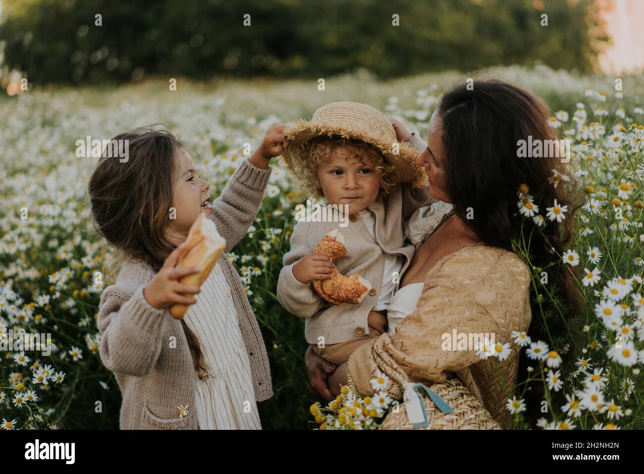 Mother and daughter looking at baby boy wearing hat amidst flowering plants Stock Photo - Alamy