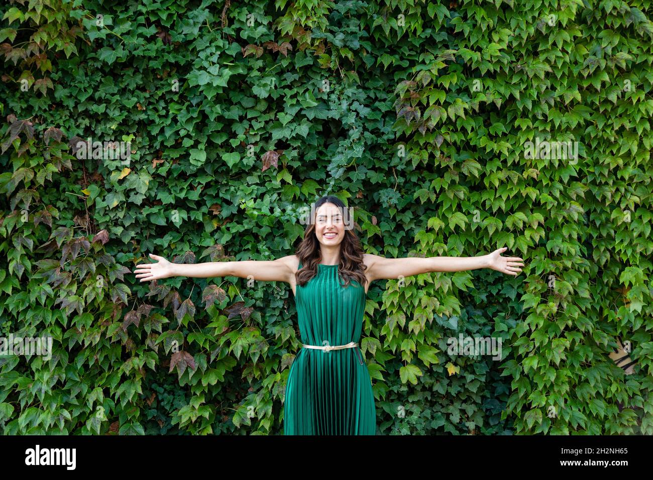 Happy beautiful woman with arms outstretched in front of ivy plants ...