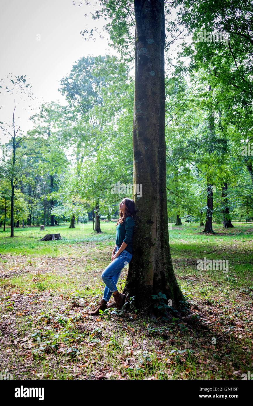 Woman leaning on tree trunk at park Stock Photo - Alamy