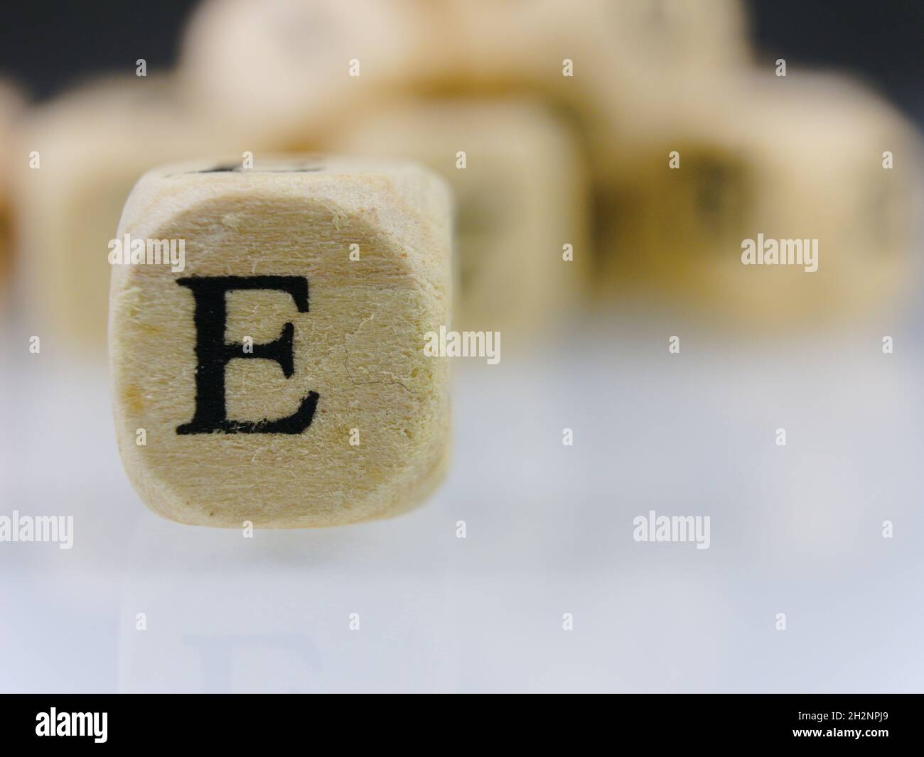 Letter E on a wooden cube with other dice letters in the background ...