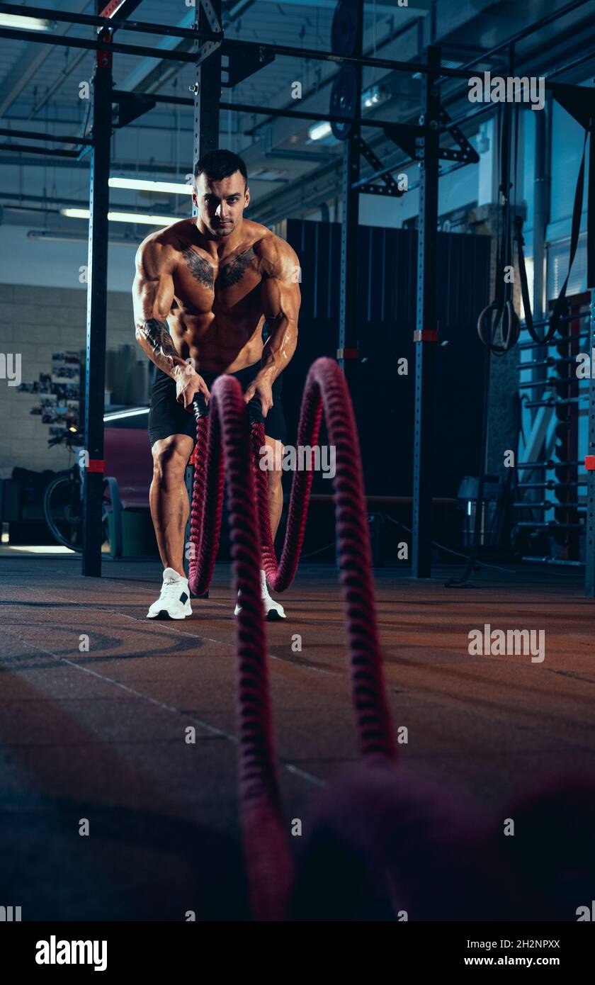 Front view of young man, muscled athlete, bodybuilder training alone at ...