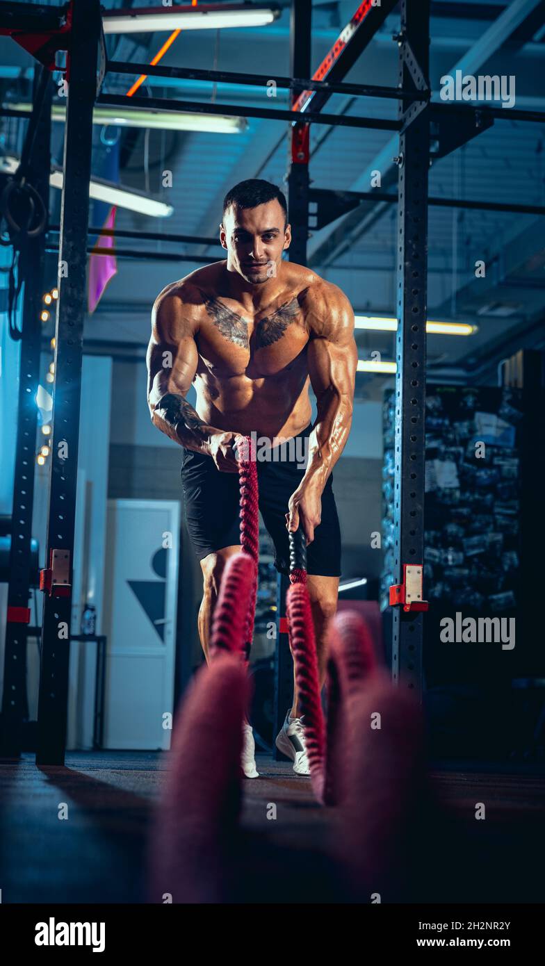 Front view of young man, muscled athlete, bodybuilder training alone at ...