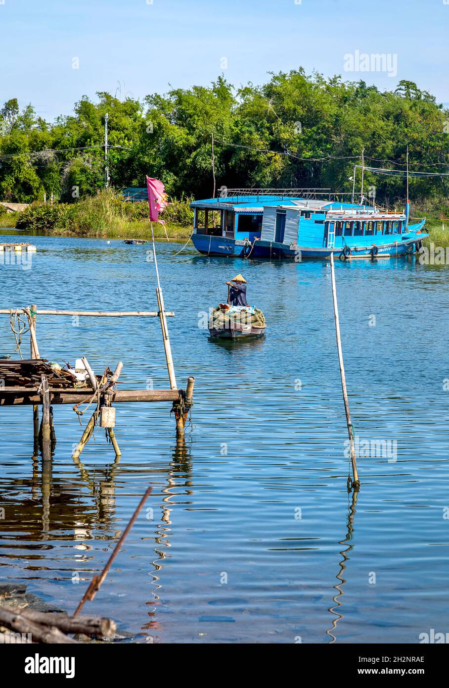 Fishing boat operator coming in wearing a conical hat in his small boat ...