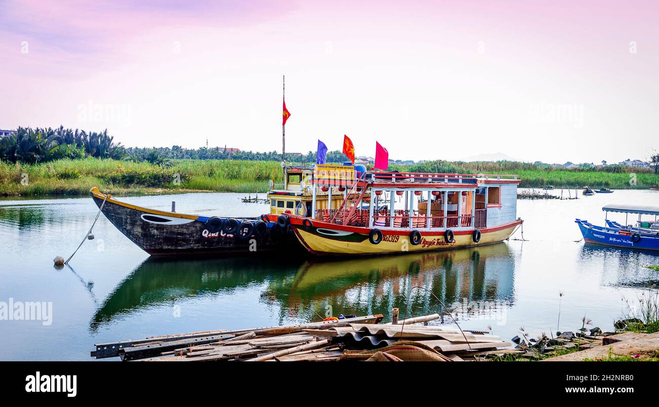 A passenger tour boat parked next to a fishing boat at Cam Kim Stock ...