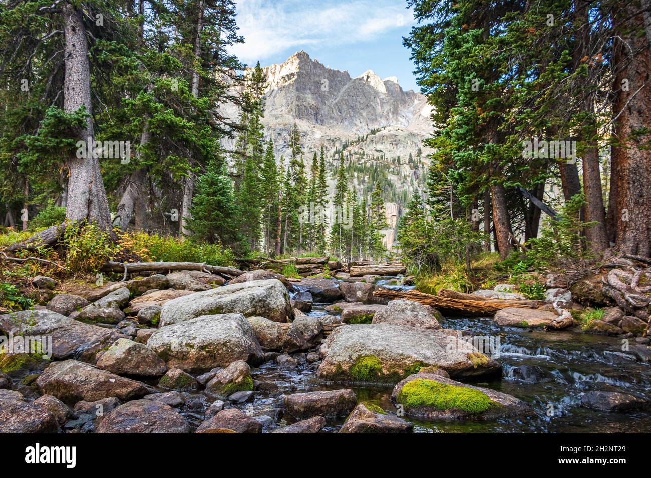 Early morning stream serenity with boulders and a rugged mountain peak ...