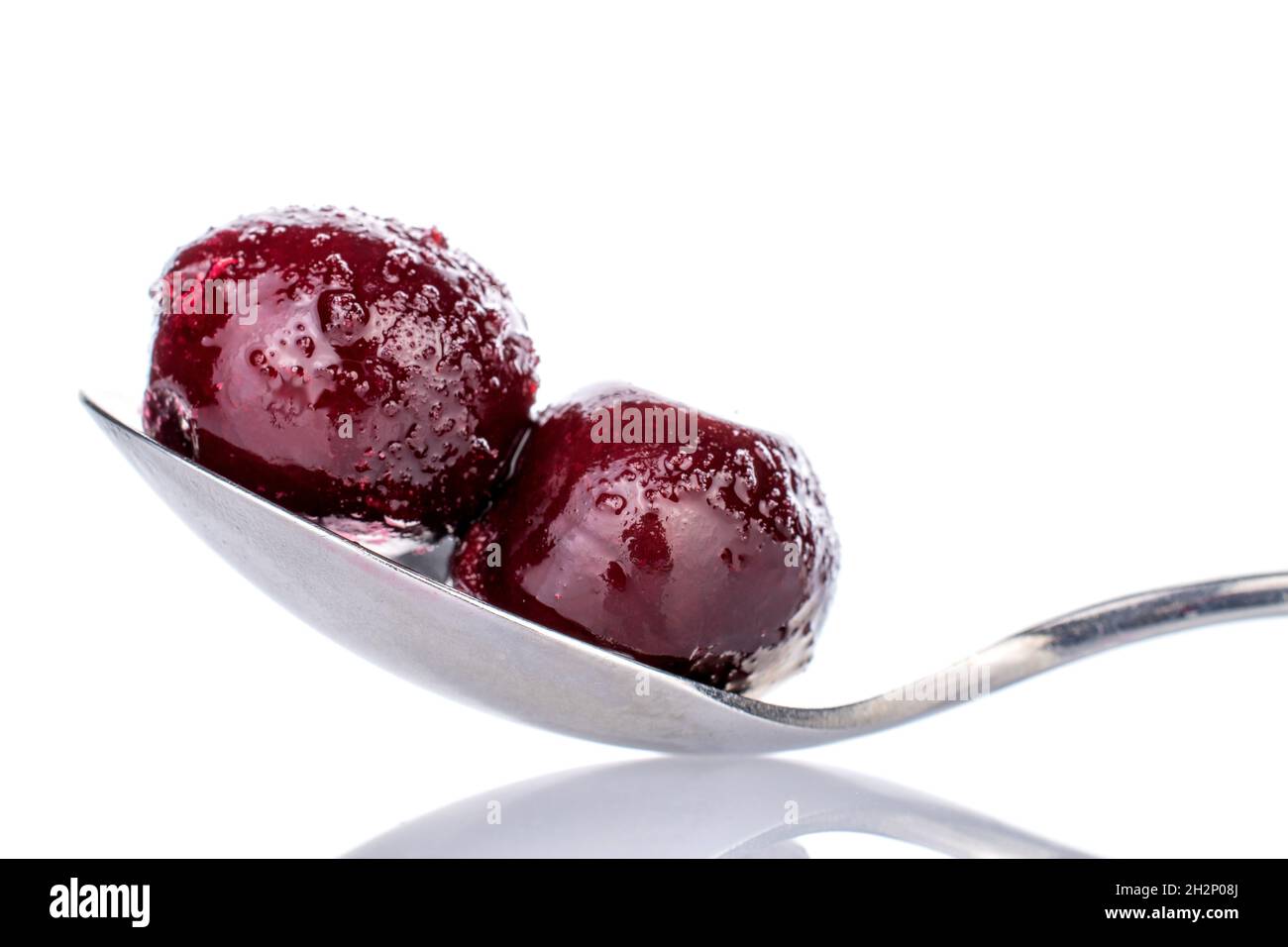 Two sweet organic frozen pitted red cherries with a metal spoon, close ...