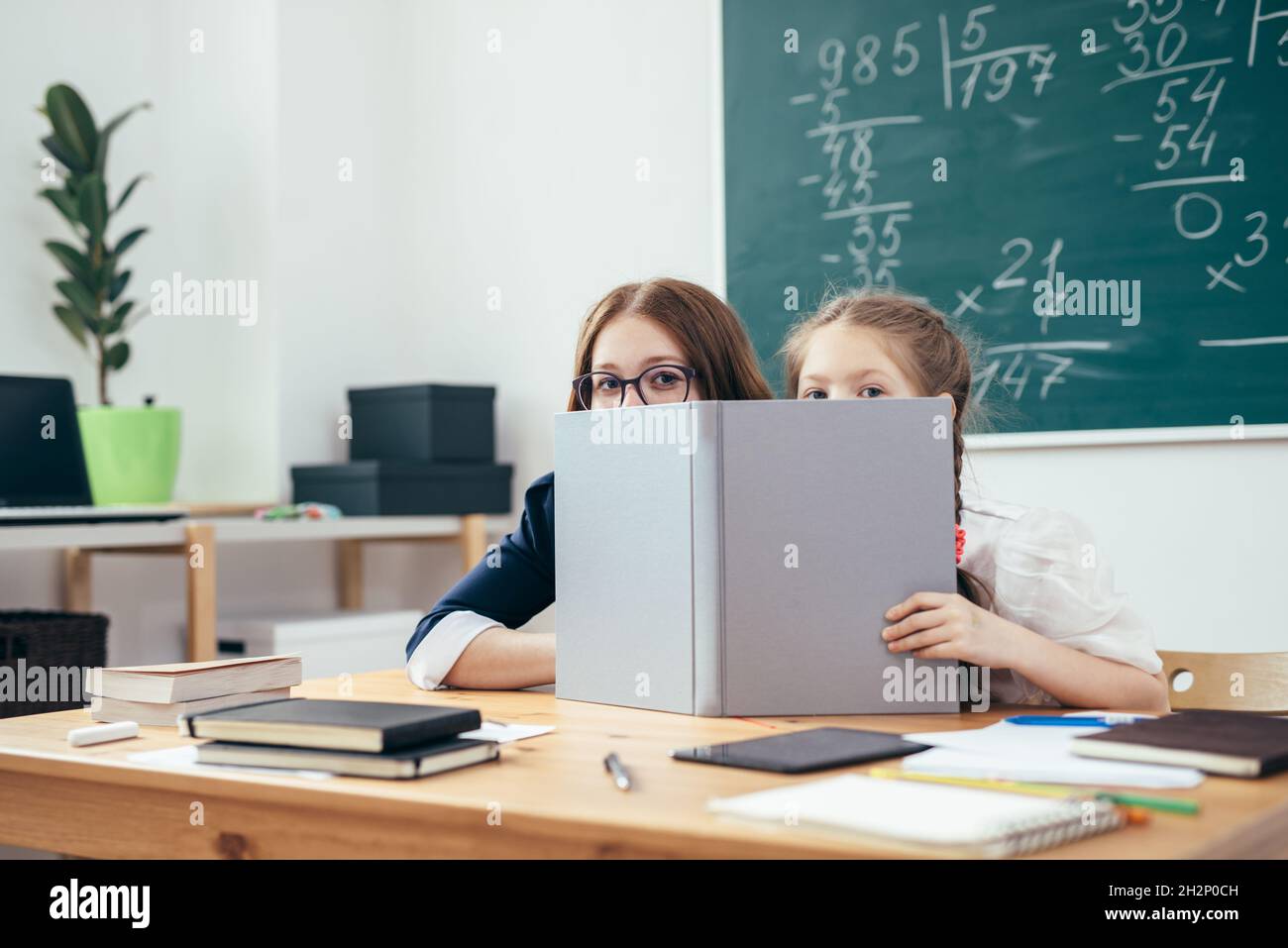 Schoolgirls hiding behind book sitting in a classroom Stock Photo - Alamy