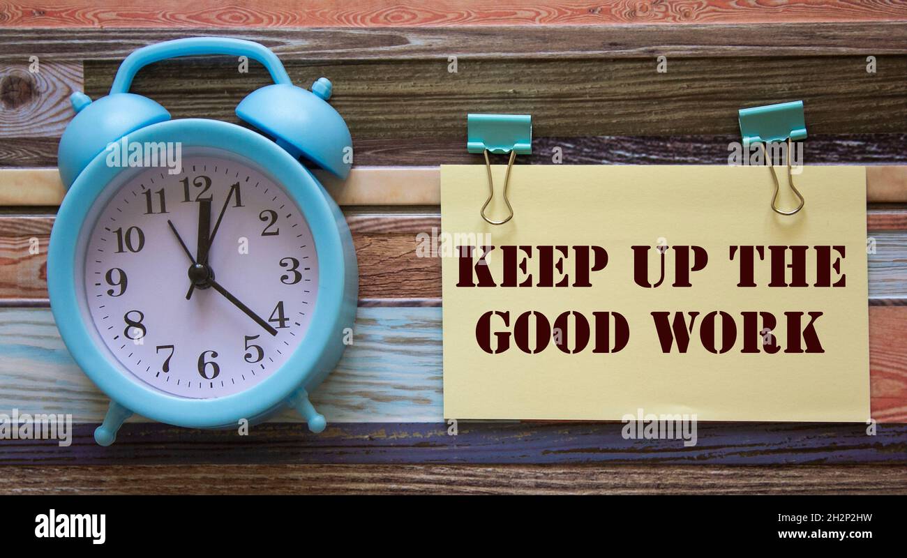 On a wooden background, an alarm clock and text keep up the good work ...