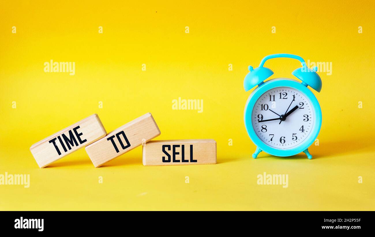 Time to Sell text on wooden blocks over yellow background with alarm ...