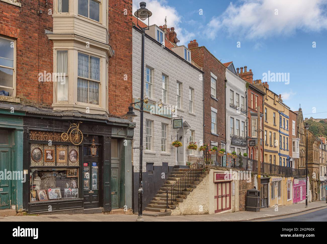 A sloping street with two levels. Steps lead up to houses and shops are ...