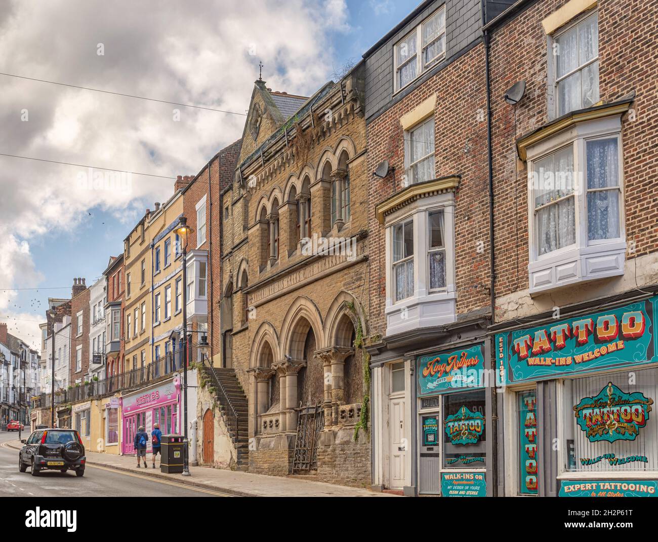A sloping street with two levels. Steps lead up to houses and shops are ...