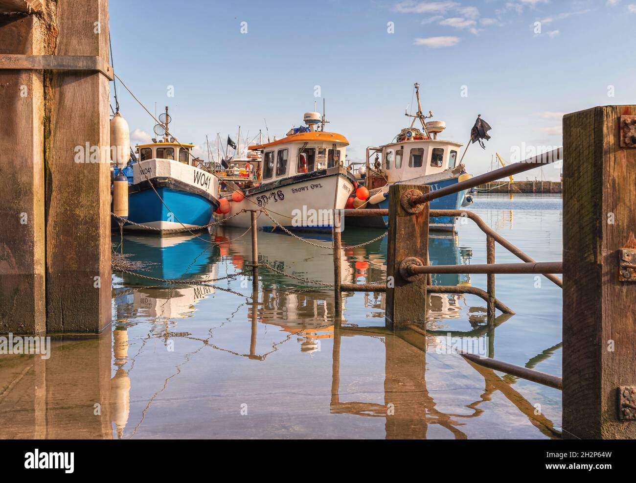 Fishing boats are moored together alongside a wharf and their ...