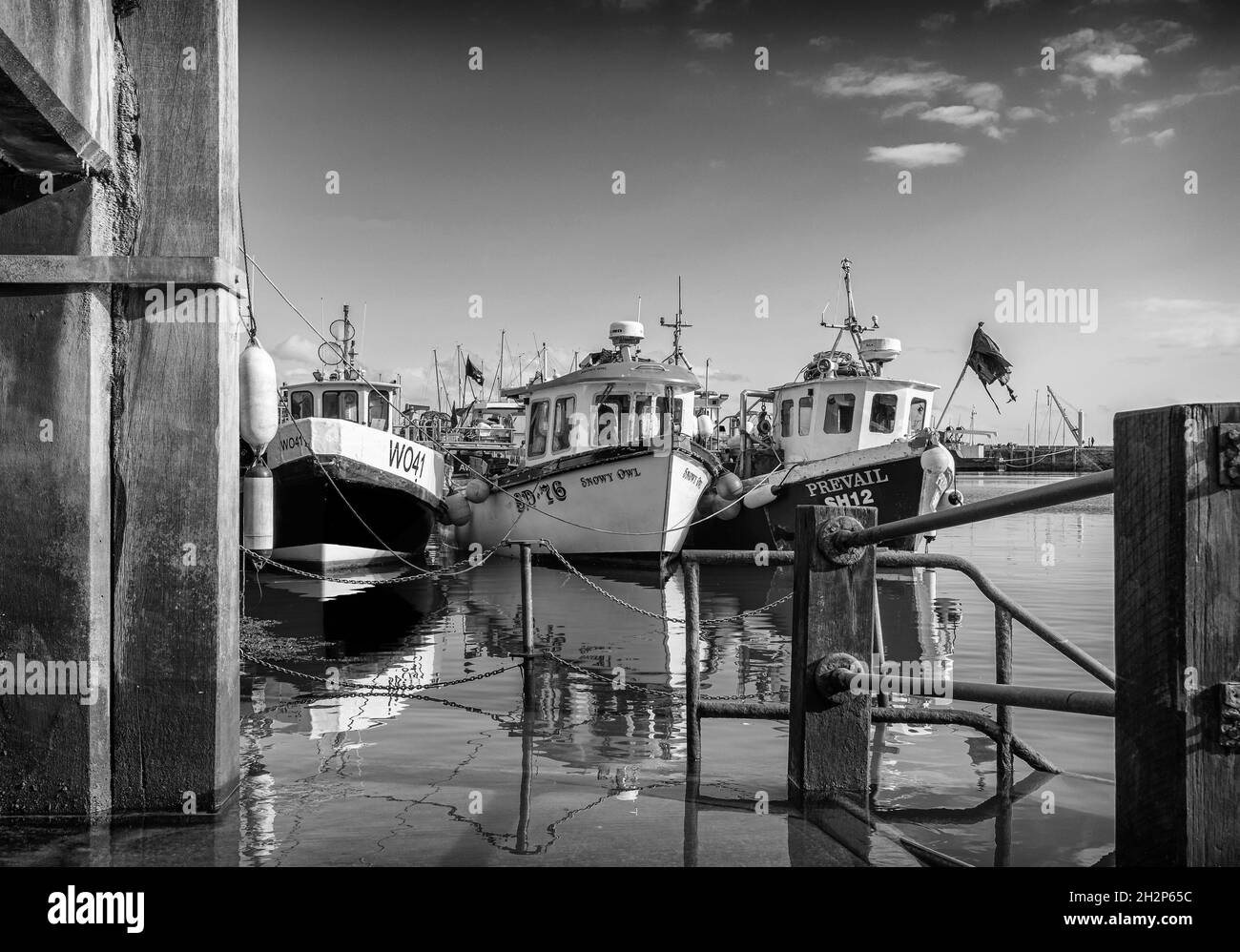 Fishing boats are moored together alongside a wharf and their ...
