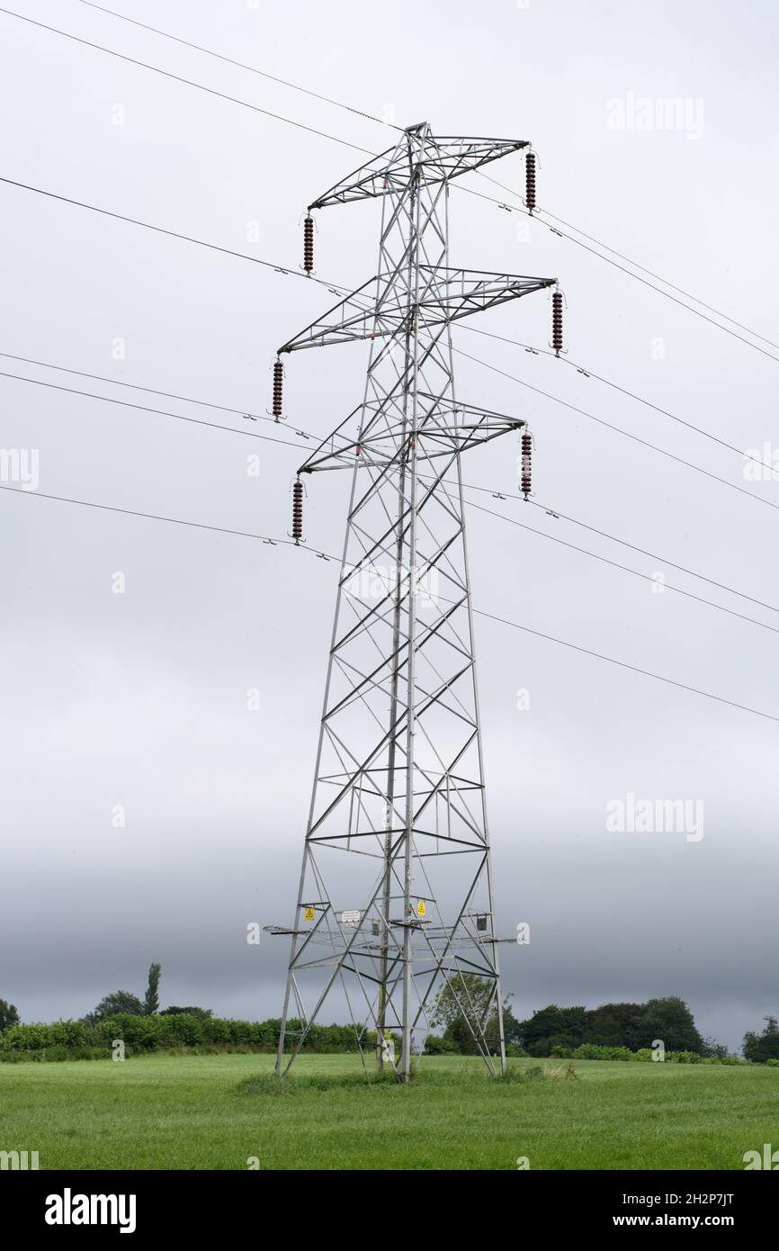 Vertical shot of a transmission tower in a field under a cloudy sky in the countryside Stock ...