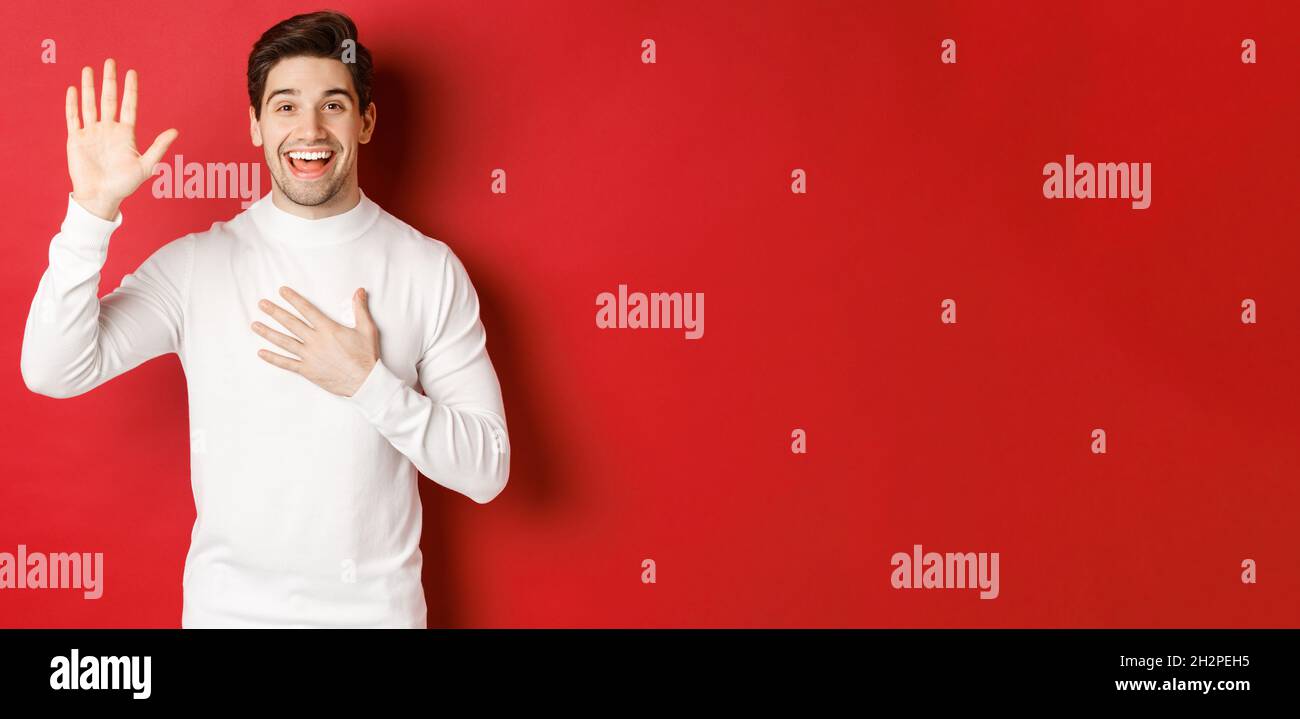 Portrait of honest smiling man in white sweater, making a promise ...