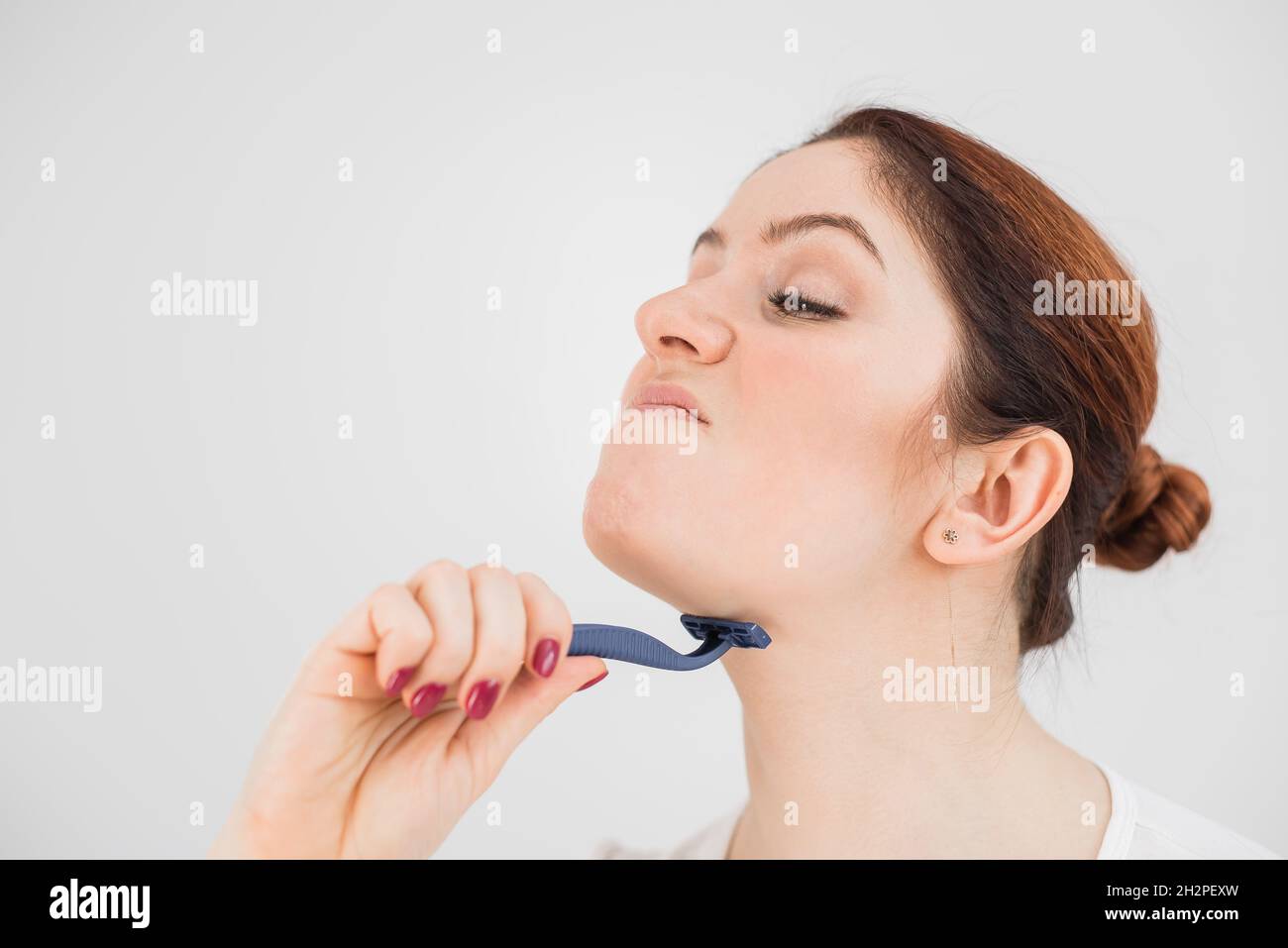 Caucasian funny woman shaves her face with a straight razor on a white ...