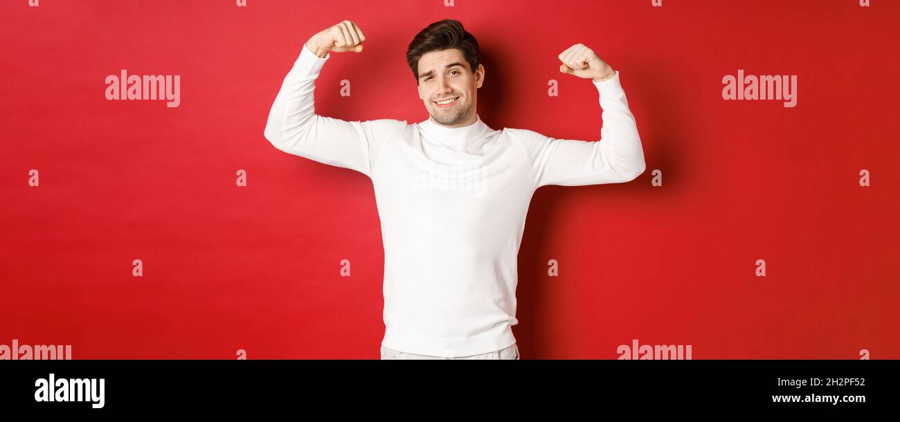 Portrait of smiling handsome man in white sweater, flexing biceps and ...