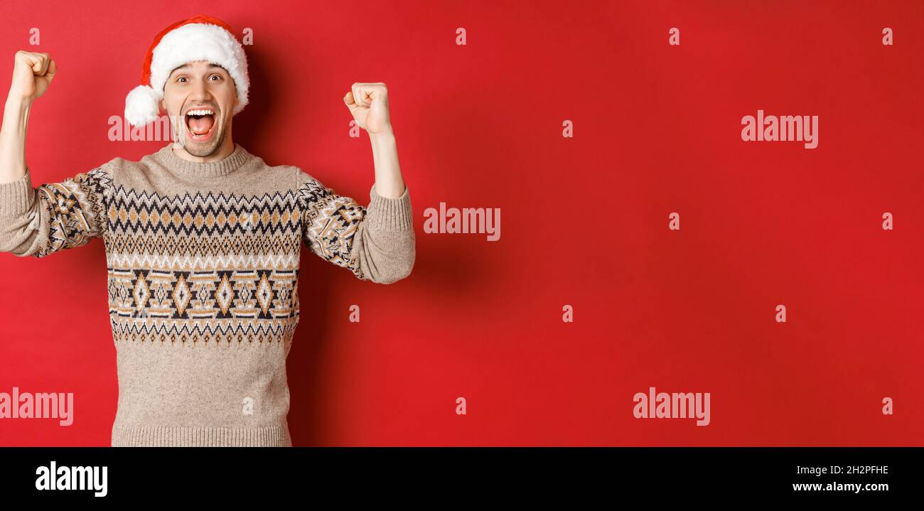 Image of cheerful handsome man in swearer and santa hat, celebrating ...