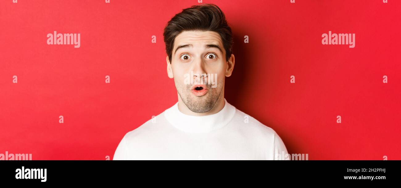 Close-up of surprised handsome man in white sweater, open mouth and ...