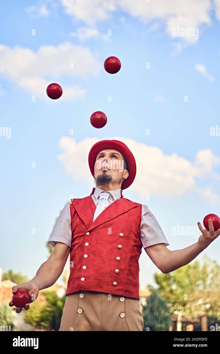 From below bearded male juggler in costume juggling red balls during ...