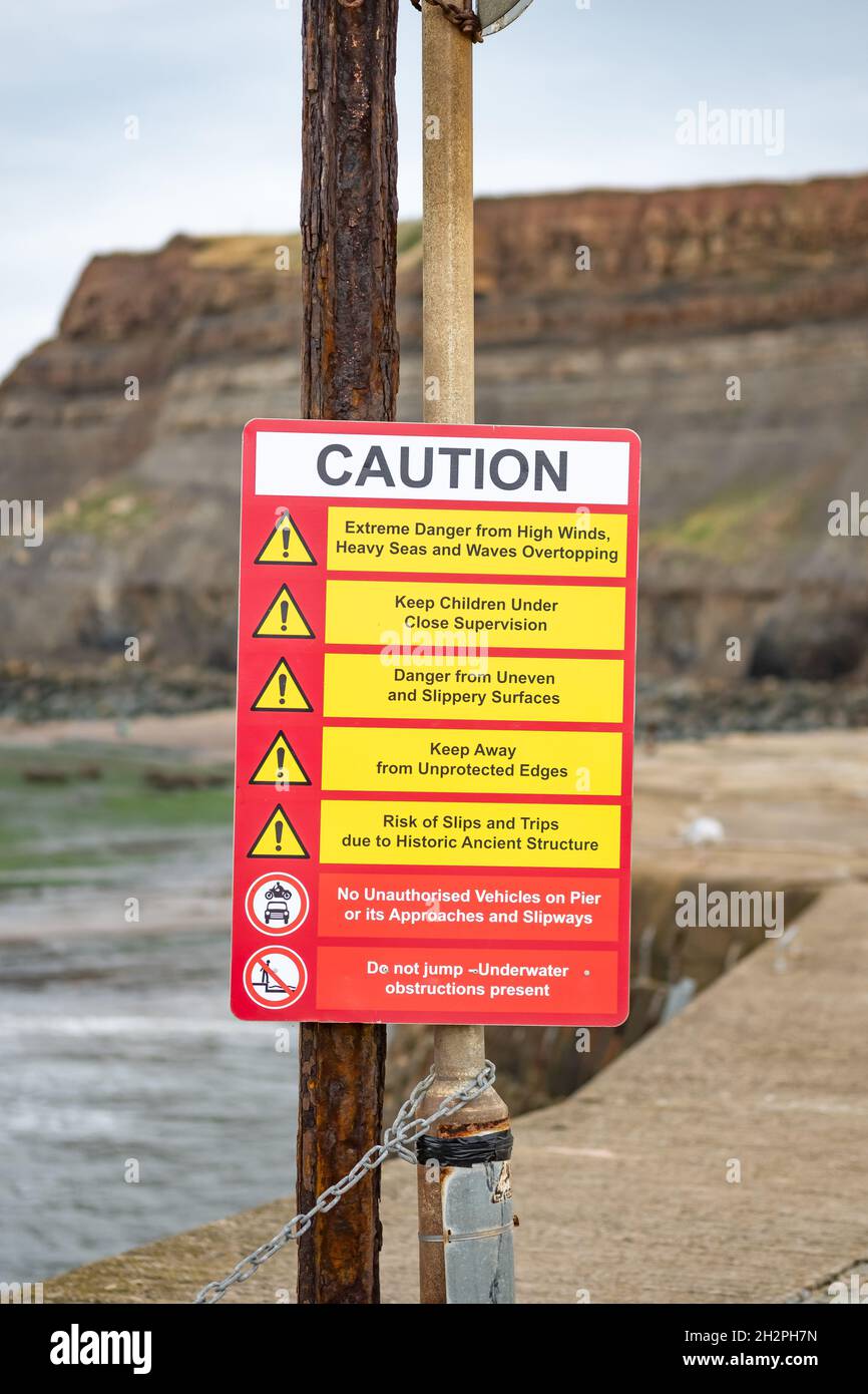 Caution sign warning people of dangers on Whitby pier Stock Photo - Alamy