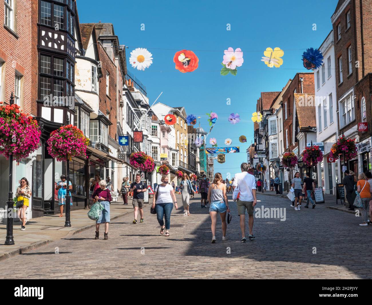 Guildford High Street shops with shoppers Autumn floral baskets and ...