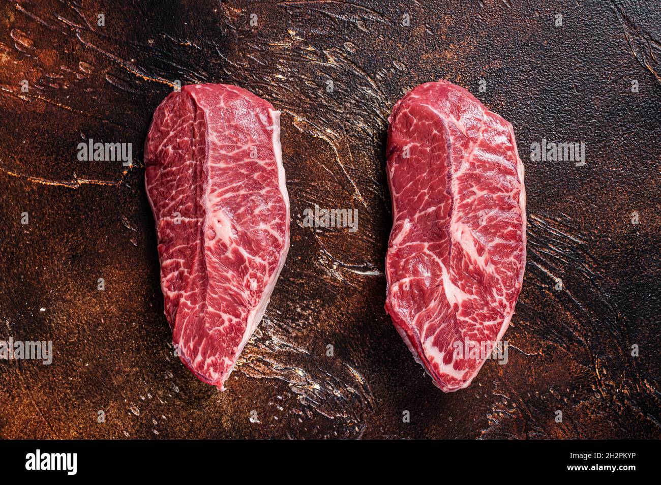 Raw Top Blade or flat iron beef meat steaks on a butcher table. Dark ...