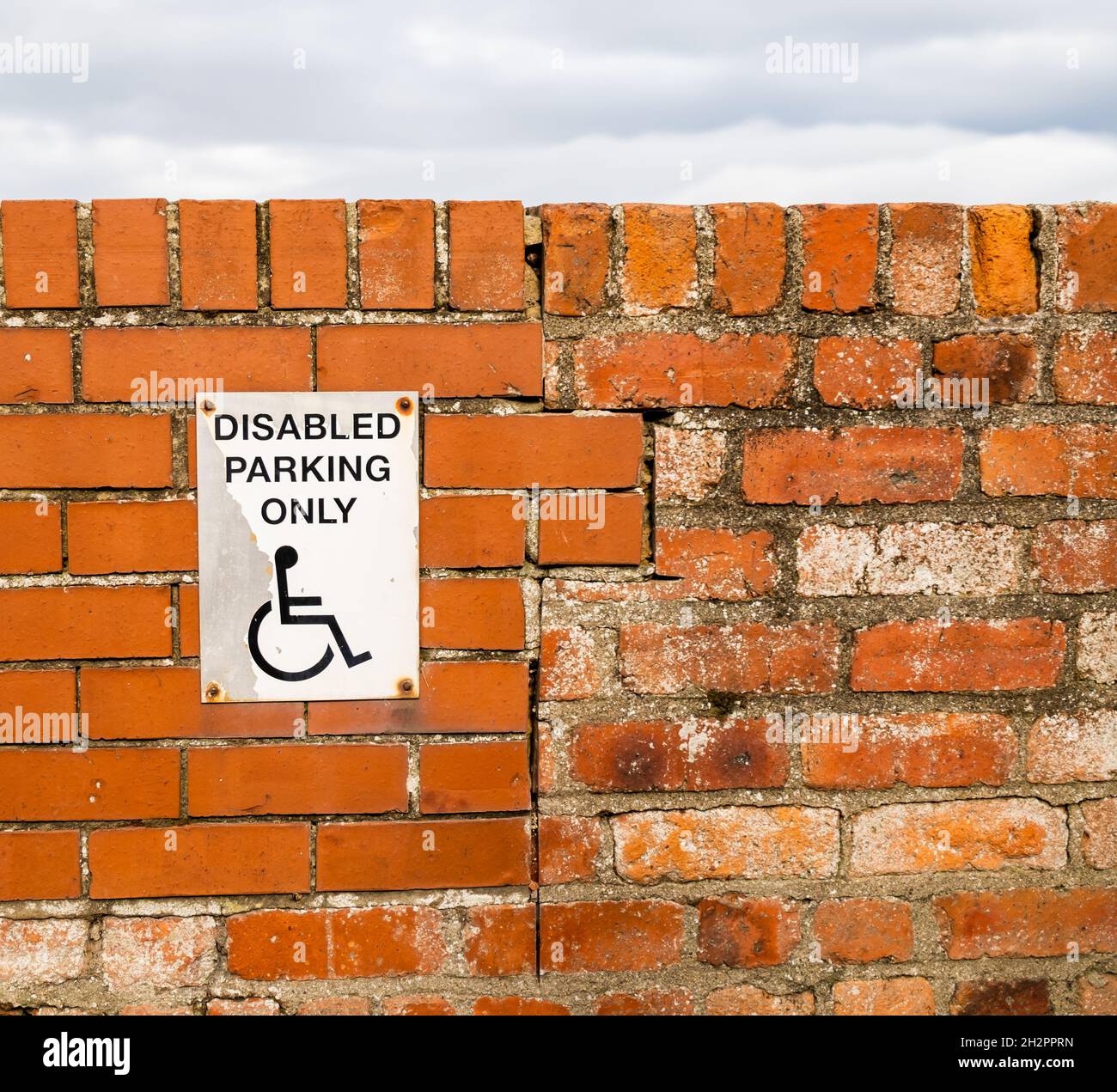 A close up of a disabled parking only sign attached to a red brick wall ...