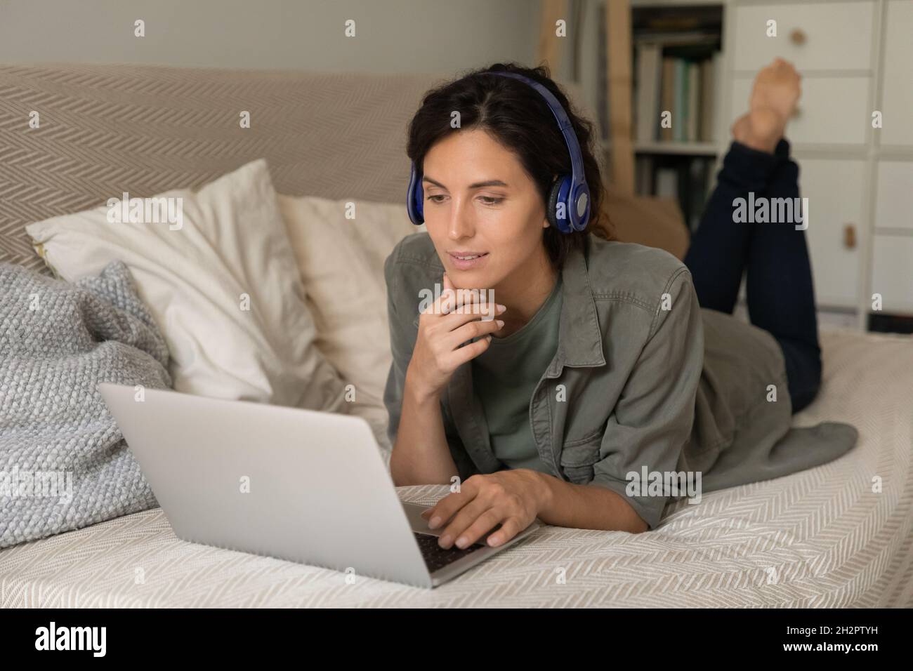 Relaxed focused female student in headphones lying on couch Stock Photo ...