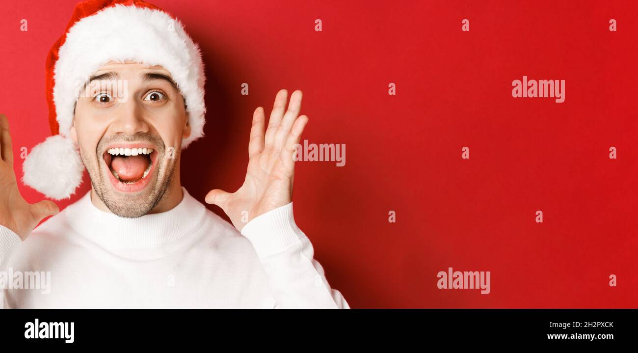 Close-up of happy young man in santa hat, making big christmas ...