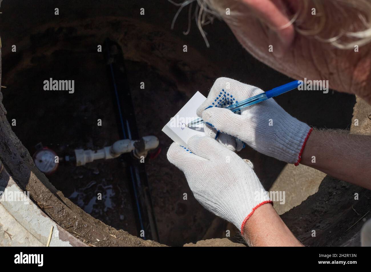 A man records the readings of the water meter, leaning over the well ...