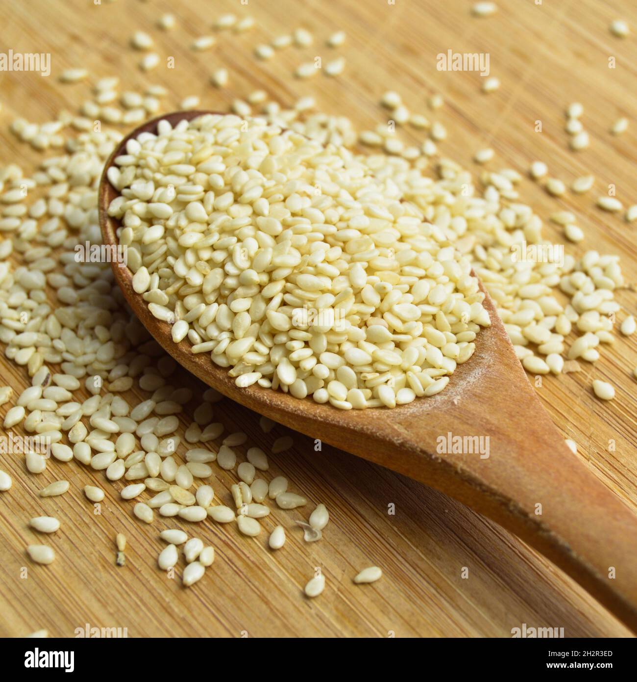 Organic fresh raw sesame seeds, in wooden spoon on bamboo cutting board ...