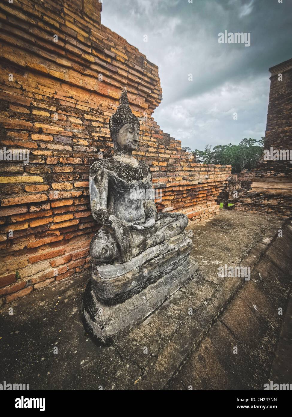 Statue of Buddha in front of the half-ruined old brick wall against a ...