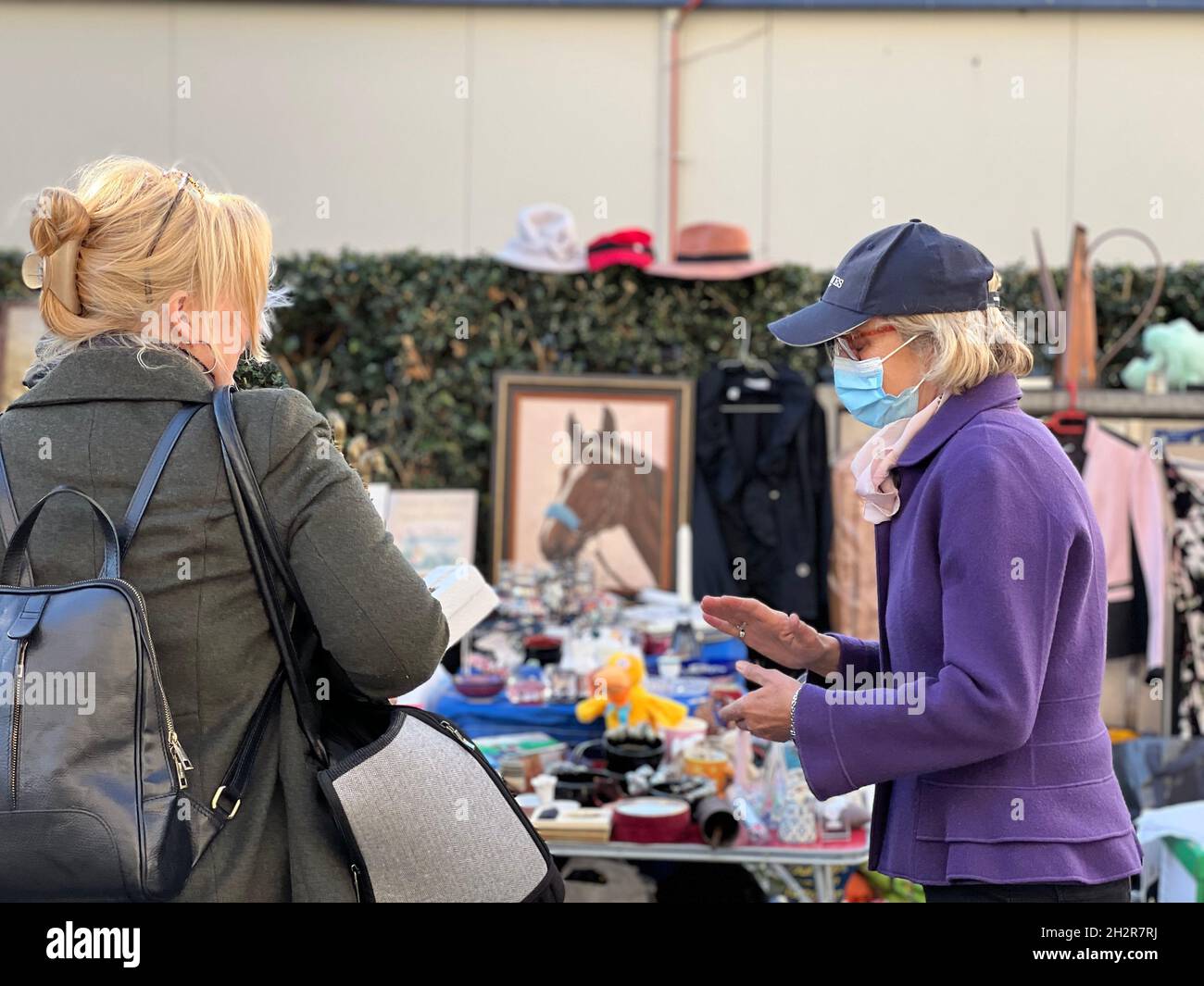 Two women having conversation at flea market. One of them is wearing a ...